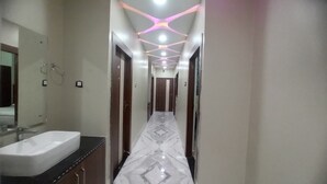 Um corredor com piso de mármore, uma pia à esquerda e portas em ambos os lados.