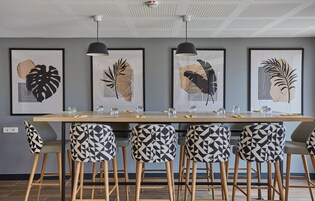 Uma sala de jantar moderna com uma longa mesa de madeira, seis cadeiras estampadas e quatro obras de arte emolduradas na parede.