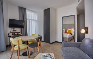 Quarto de hotel moderno com área de refeições, sofá, televisão e cama com espelho.