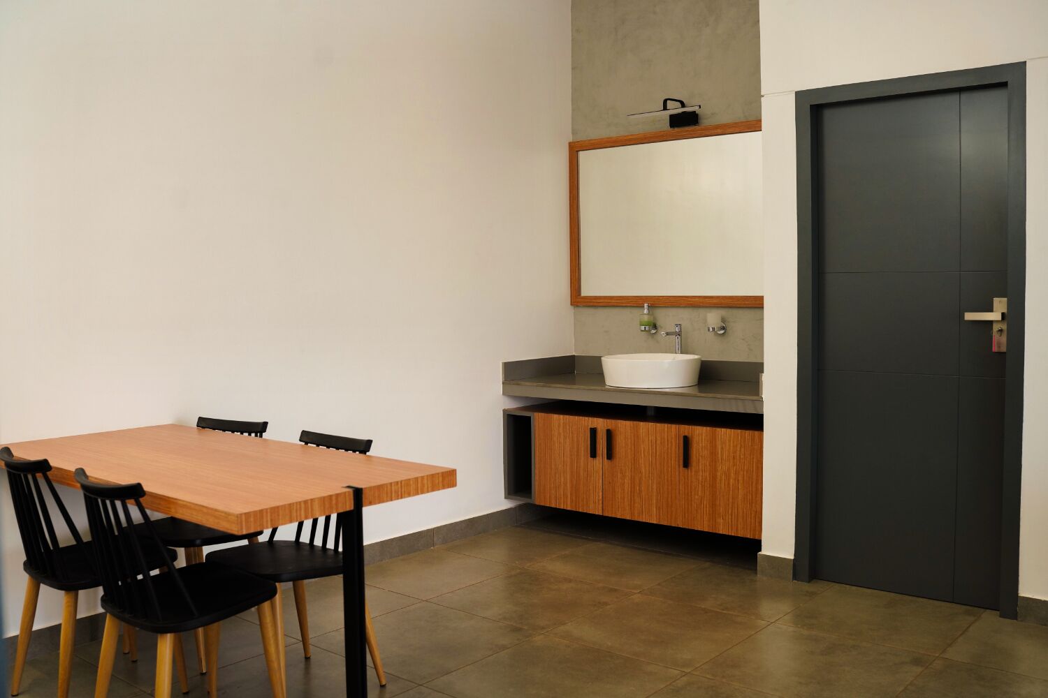 Quarto pequeno e moderno, com uma mesa de jantar de madeira e cadeiras, pia embutida e uma porta escura.
