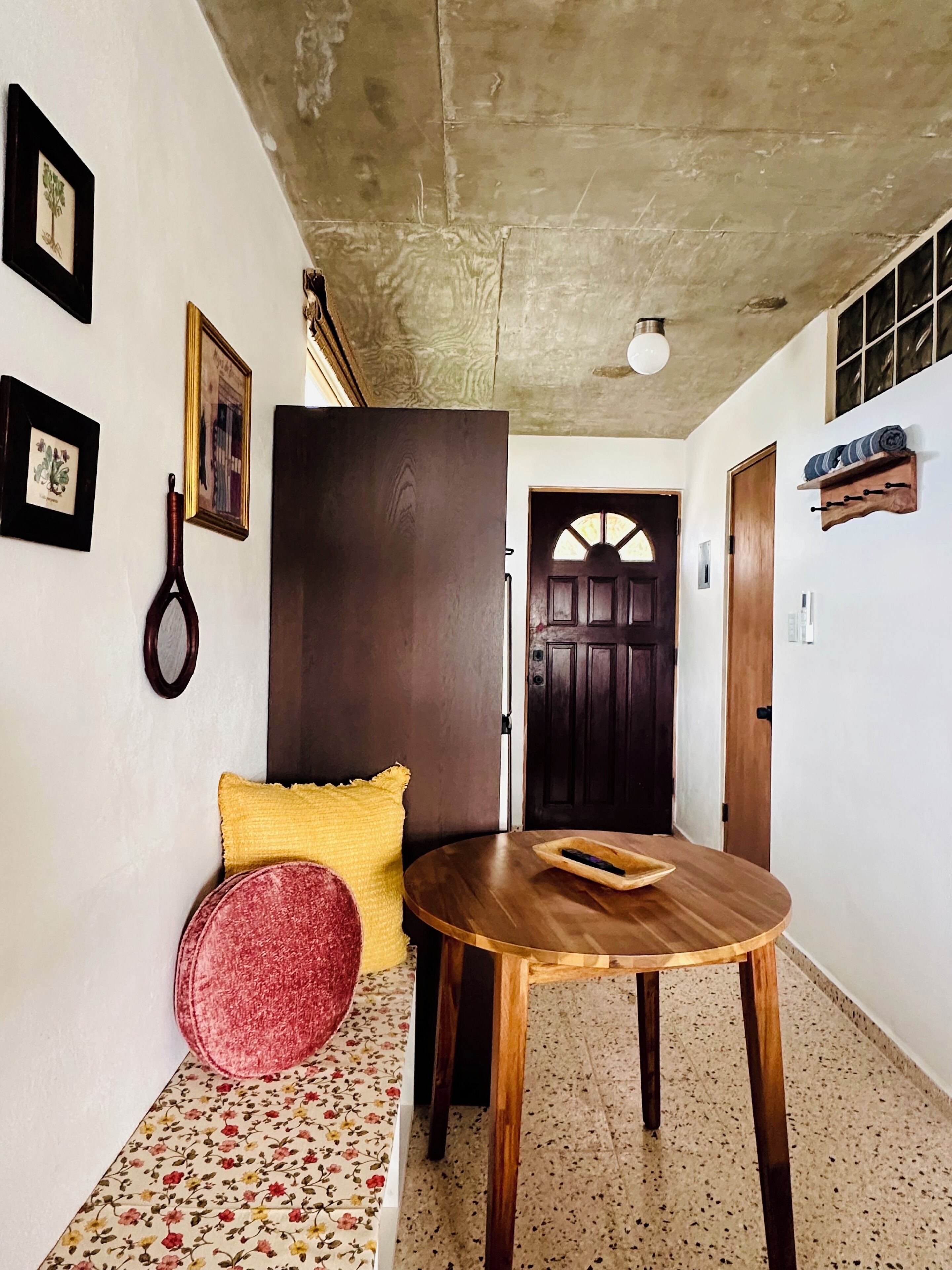 Um corredor com uma mesa redonda de madeira, uma porta de madeira escura e um almofado amarelo.