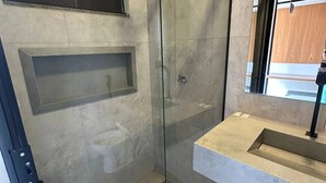Uma casa de banho moderna com cabine de duche em vidro, sanita embutida e espelho com lavatório.