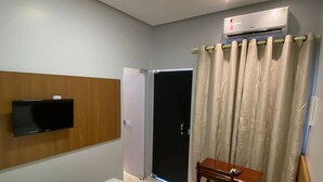 Quarto com televisão de tela plana fixada em um painel de madeira, aparelho de ar condicionado, porta e cortina.