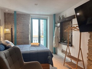 Quarto com cama, cadeira, televisão, varanda e parede de pedra.