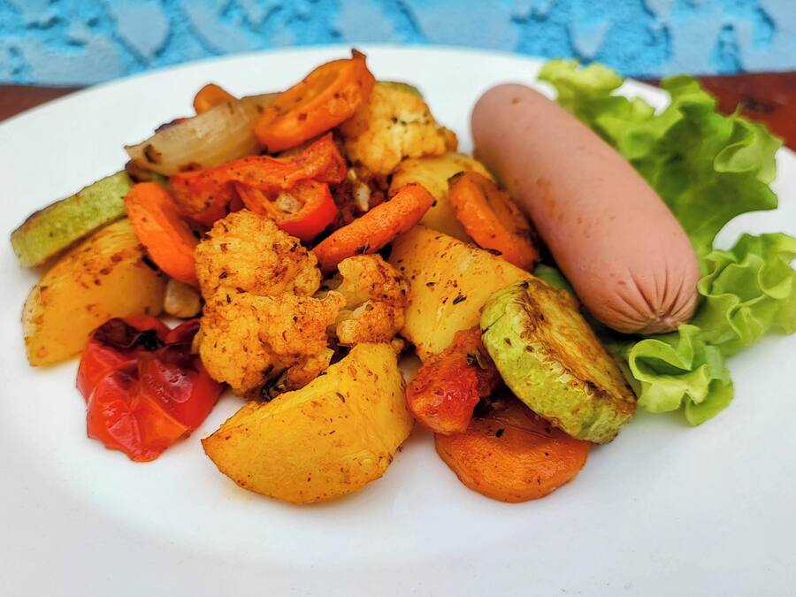 Um prato com legumes assados e uma salsicha.