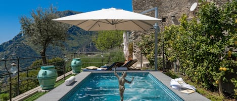 Uma área de piscina com uma estátua, cadeiras de descanso e vista para montanhas.
