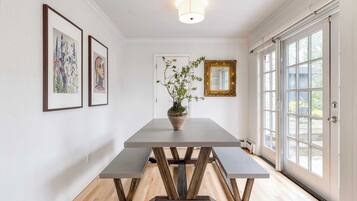 Uma área de refeições com mesa e bancos, um vaso com flores, obras de arte emolduradas na parede e uma janela grande com vista.
