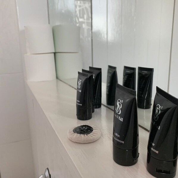 Um banheiro com bancada branca exibindo diversos produtos de higiene pessoal pretos, incluindo uma garrafa rotulada “Jasmine” e vários saquinhos com um logotipo.