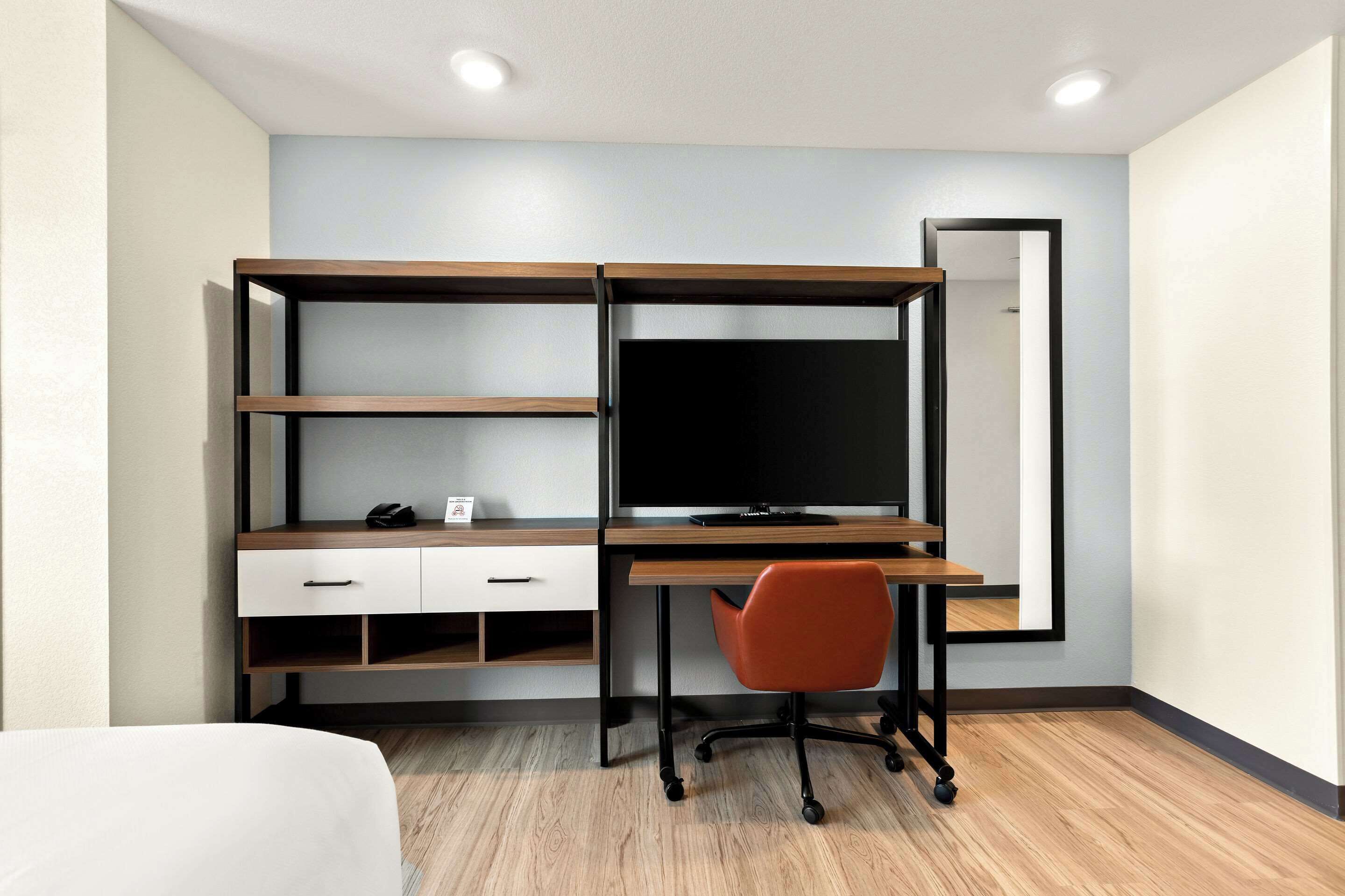 Quarto de hotel moderno com uma mesa de madeira, uma cadeira preta, televisão de tela plana e um espelho grande.