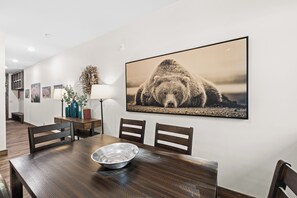 Uma sala de jantar com uma mesa de madeira, cadeiras, uma tigela de metal e uma grande fotografia de um urso na parede.