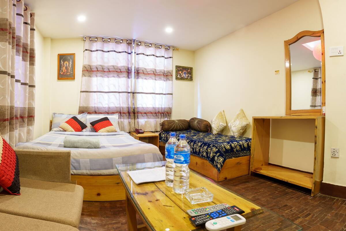 Quarto de hotel com cama, sofá, mesa de centro e mesa de cabeceira de madeira.