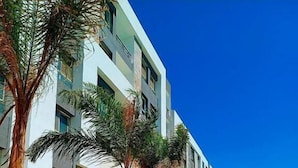 Um hotel moderno com vários andares, áreas de estar ao ar livre com espreguiçadeiras e palmeiras.