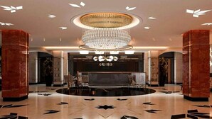 Um lobby moderno com um lustre central, colunas de mármore e um balcão de recepção.