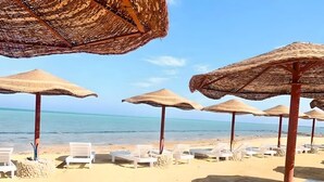 Uma praia com fileiras de cadeiras de praia brancas e guarda-sóis de palha.