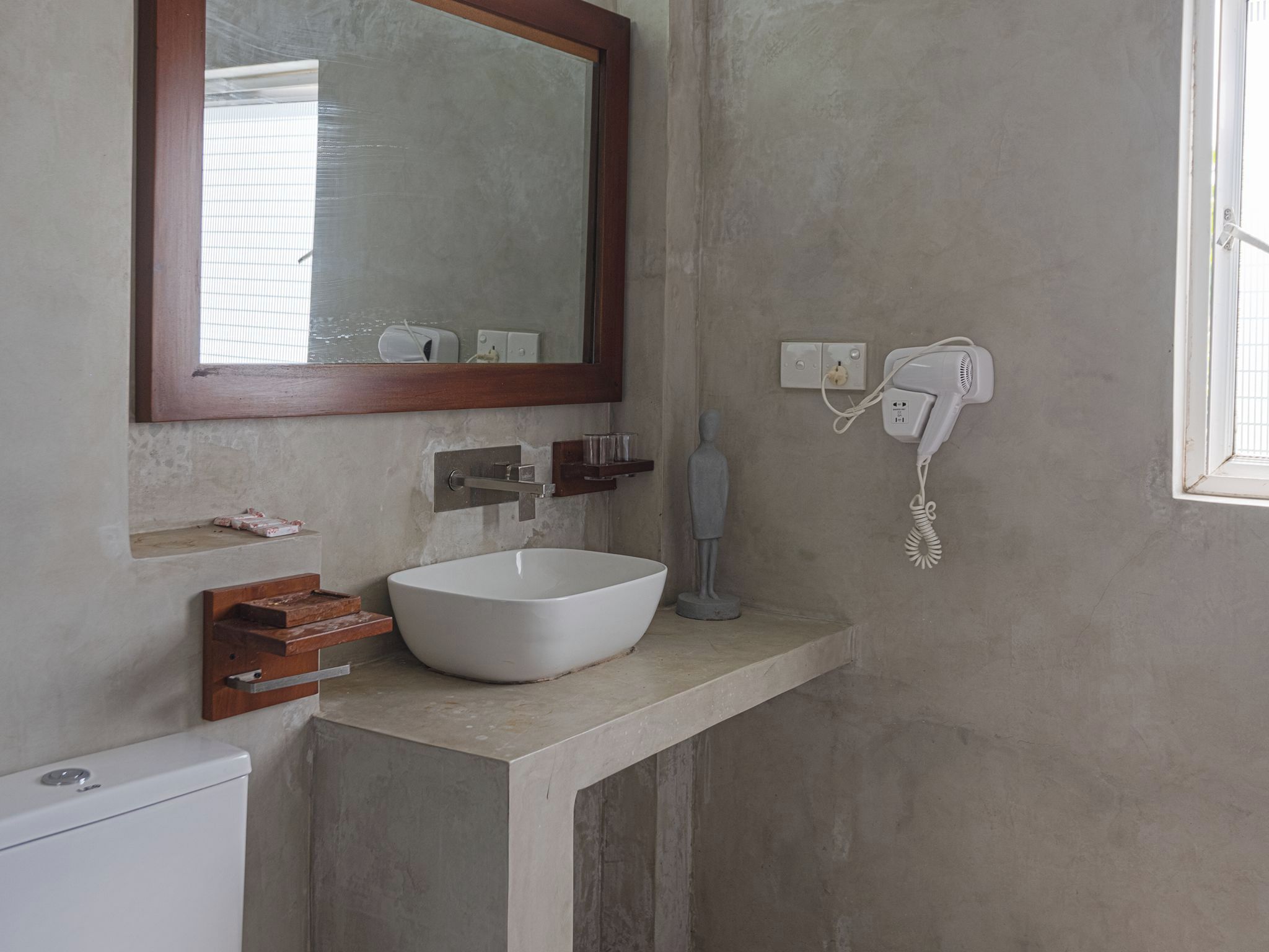 Casa de banho com lavatório branco, espelho, secador de cabelo e telefone fixo na parede.