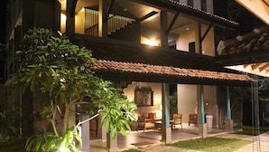 Um edifício de dois andares com varanda coberta, área de estar ao ar livre e um jardim bem cuidado.