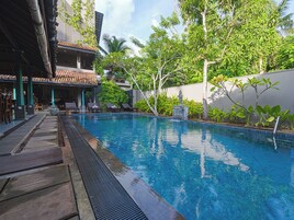 Piscina com deck revestido, espreguiçadeiras e uma estátua.