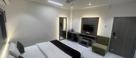 Quarto de hotel moderno com uma cama grande, uma TV de tela plana na parede, área de estar com uma mesa pequena e cadeiras, e uma porta com design único.