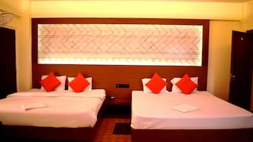 Quarto de hotel com duas camas, cada uma com roupa de cama branca e almofadas vermelhas, uma janela grande com padrão geométrico e cabeceira de madeira.