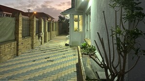 Um pátio estreito e pavimentado, com chão de azulejos, portão e uma pequena área ajardinada com planta em vaso.