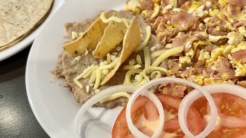 Um prato com feijão, ovos, presunto, queijo e tomate sobre uma mesa.