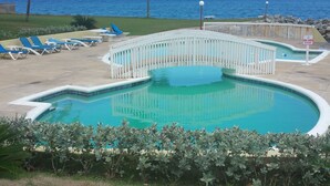 Uma área de piscina com borda curva, espreguiçadeiras e palmeiras.