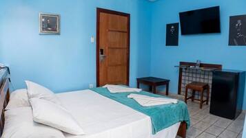 Quarto com uma cama, uma escrivaninha, uma televisão e uma porta.