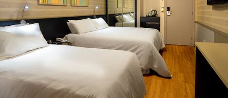 Quarto de hotel com duas camas, uma escrivaninha, televisão e espelho.