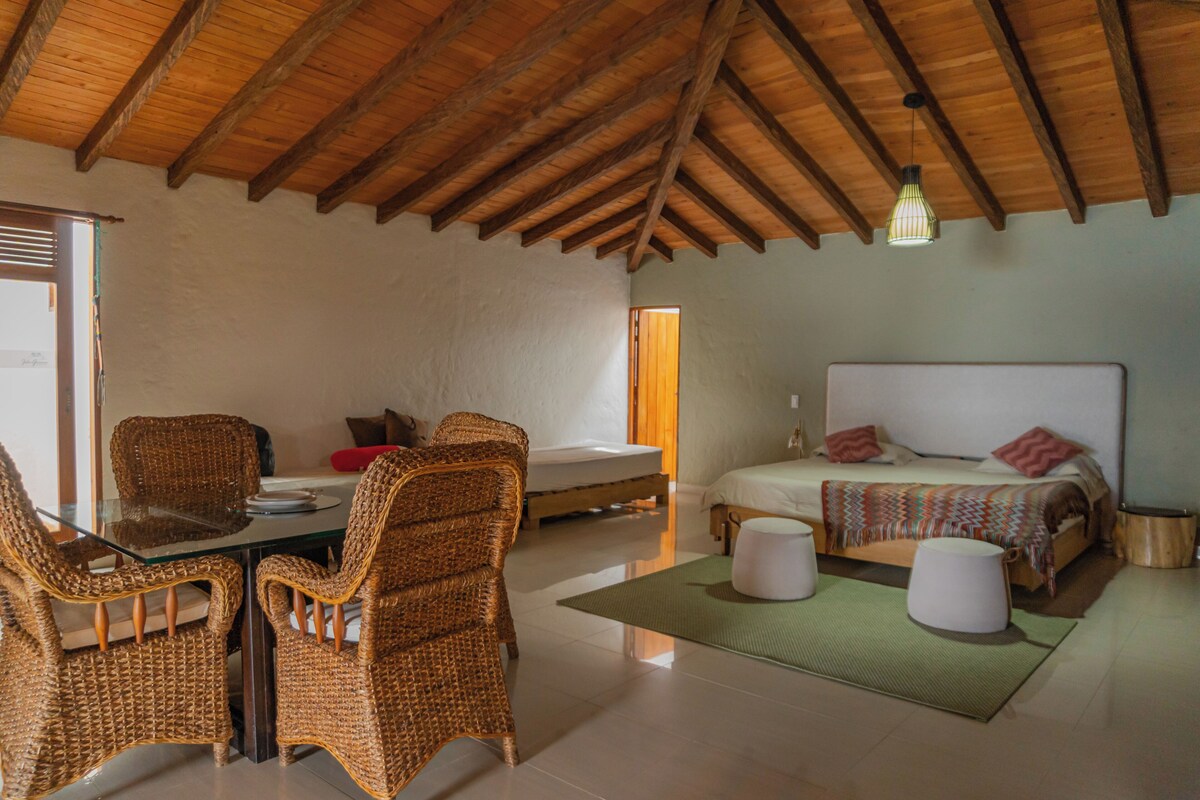 Quarto com teto de madeira, cama com almofadas, mesa com cadeiras e uma pequena mesa redonda.