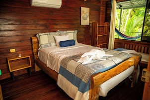 Quarto de cabana de madeira com cama, rede e janela com vista para vegetação.