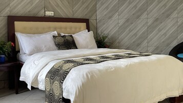 Cama bem arrumada com manta estampada, cabeceira e mesa de cabeceira com uma planta.