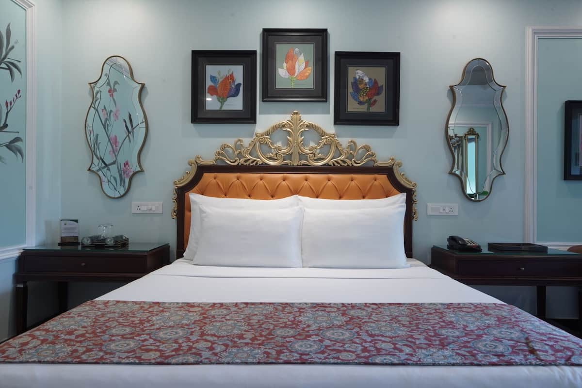Uma cama com cabeceira estofada, colcha estampada e três quadros de flores na parede.