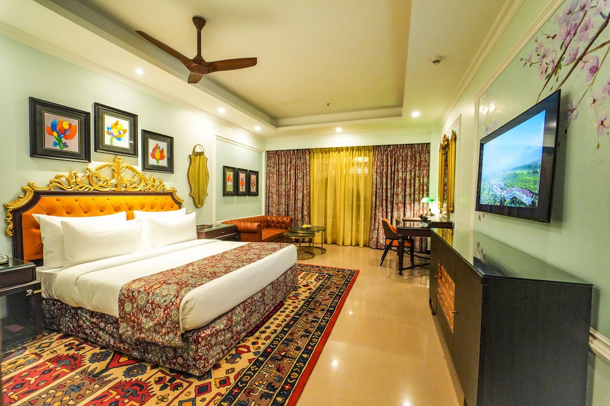 Quarto de hotel com uma cama grande, uma escrivaninha, uma cadeira, uma televisão e um ventilador de teto.