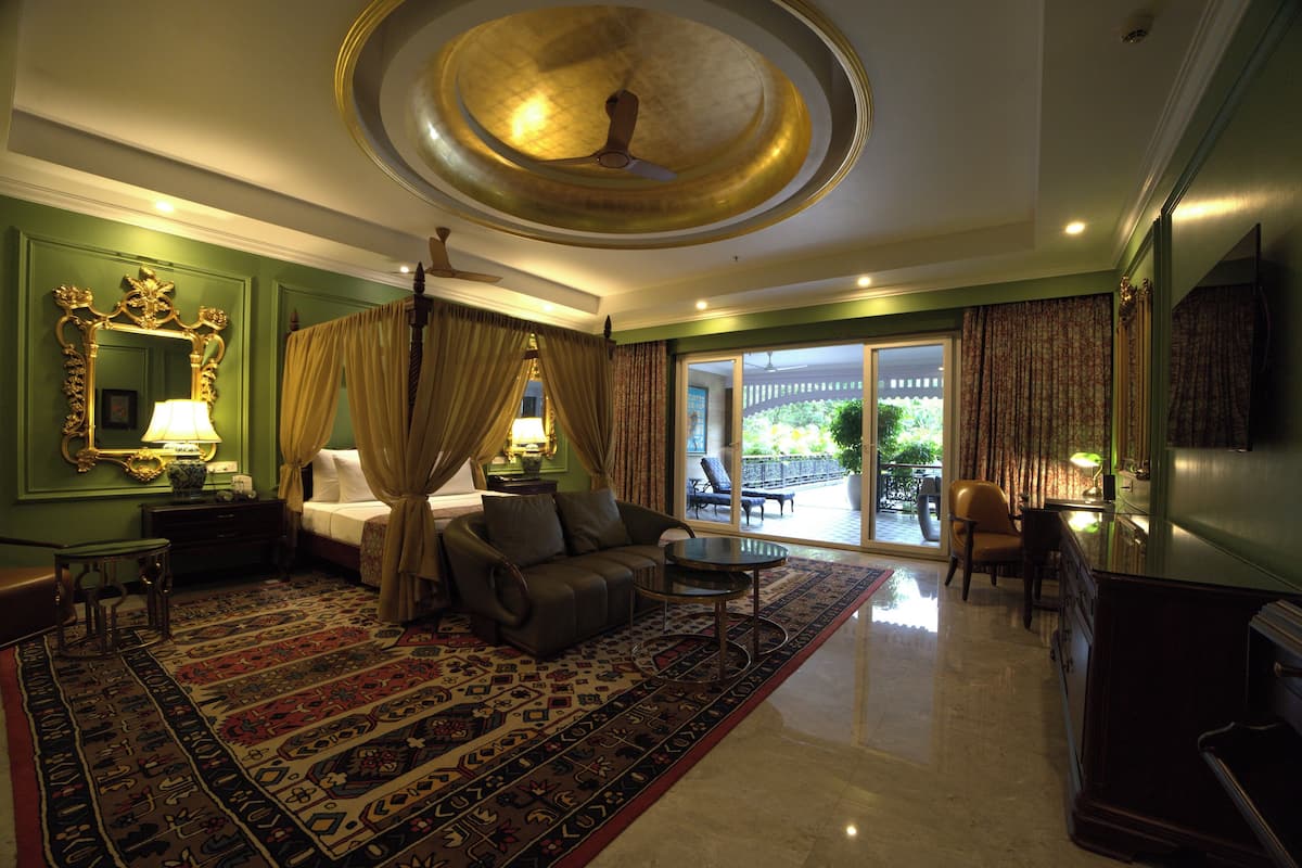 Um quarto espaçoso com uma cama grande, um espaço de estar com sofá e poltronas, uma mesa de centro e vista para o exterior através de uma porta de vidro deslizante.