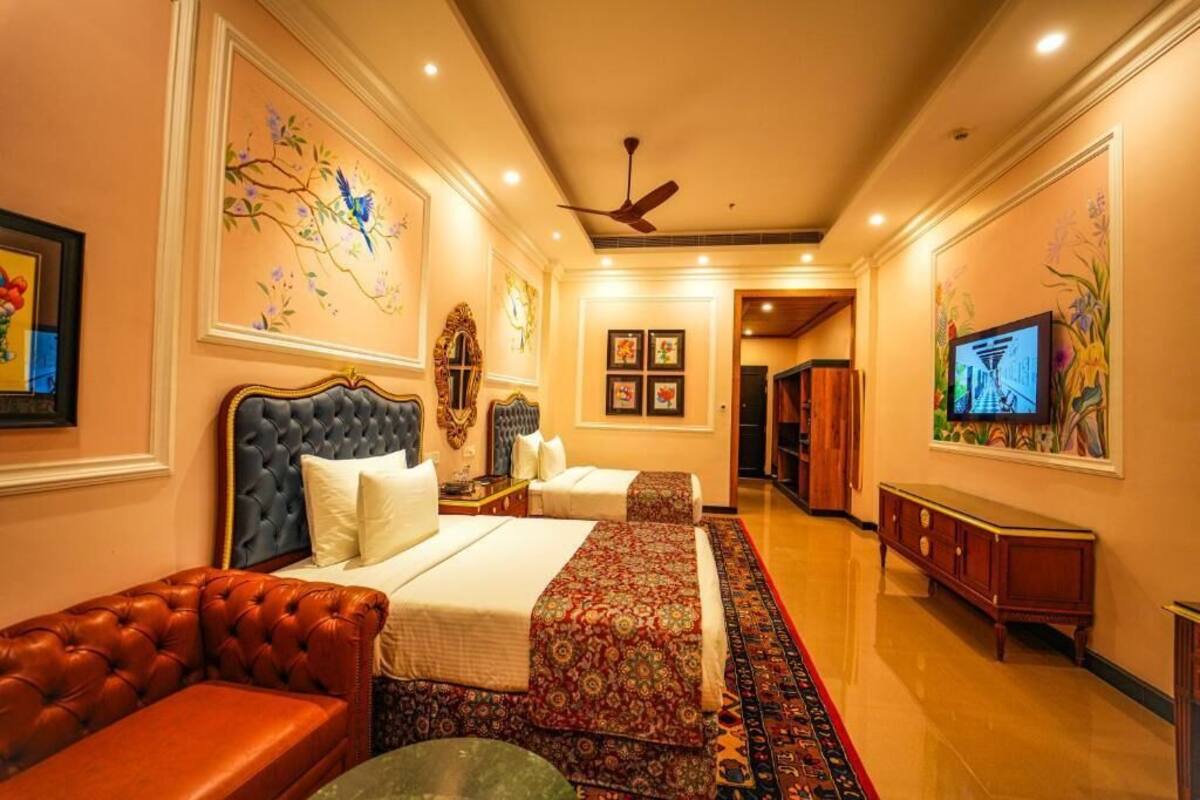 Quarto de hotel com uma cama grande, um sofá, uma televisão e uma parede decorativa.