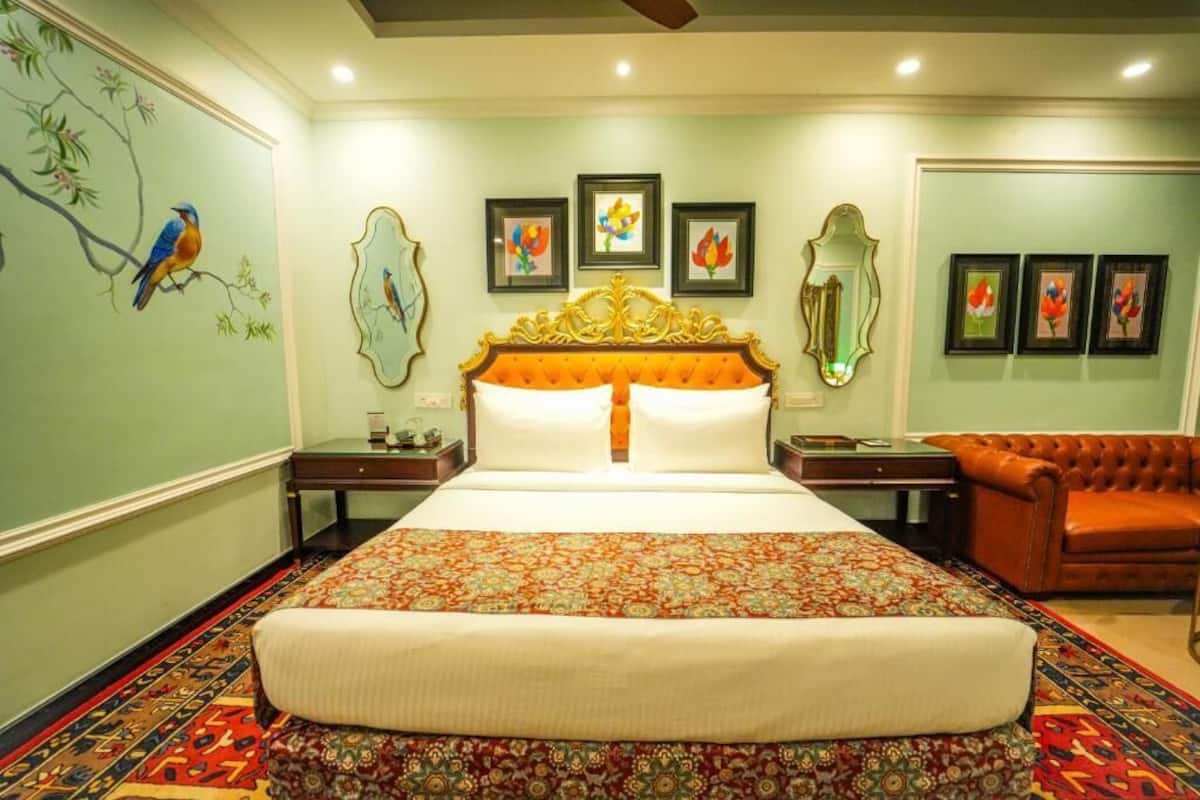 Quarto com uma cama grande, um chaise longue, parede com obras de arte emolduradas e um espelho decorativo.