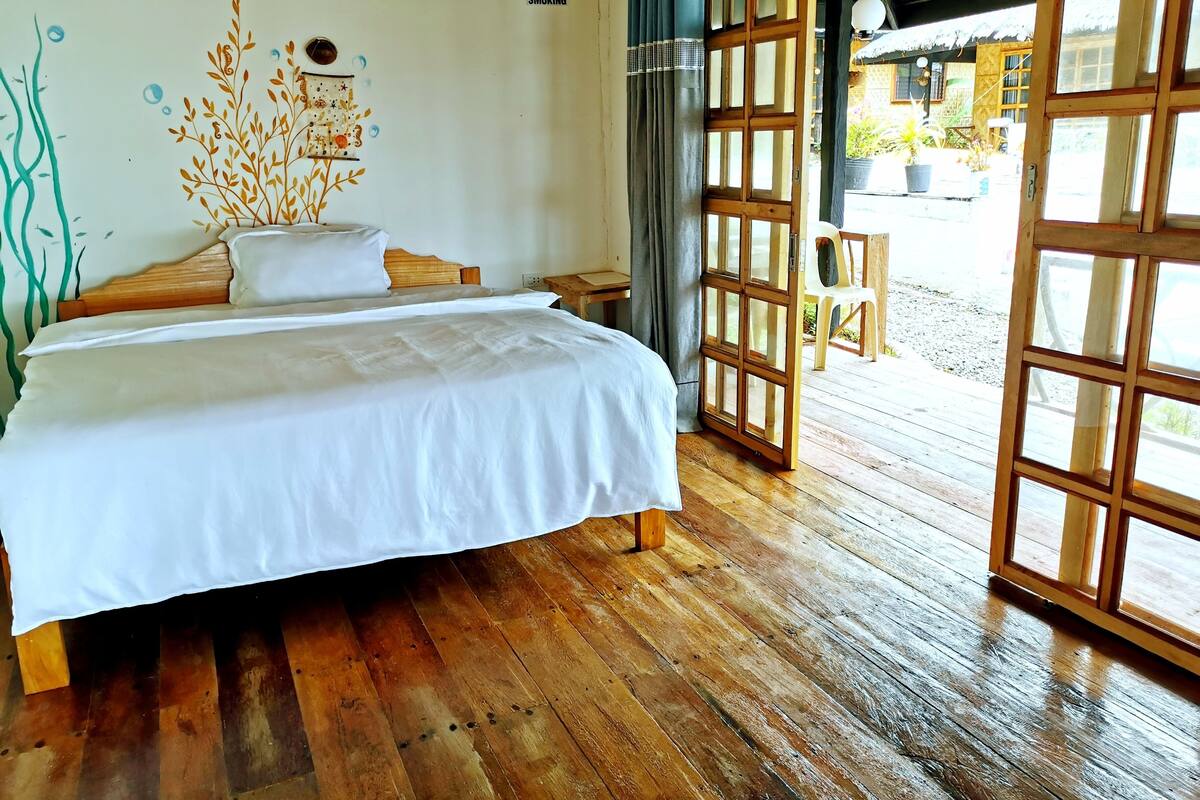 Quarto com estrutura de madeira, uma cama e um aviso de 'Não Fumar', com vista para o exterior.