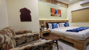 Quarto de hotel com cama, sofá, mesa de cabeceira e uma pequena mesa.
