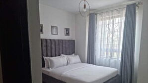 Quarto com cama, cabeceira, janela com cortinas e parede com quadros.