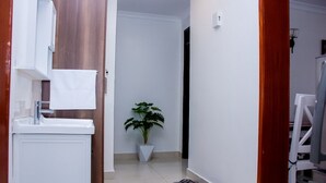 Corredor com pia branca, planta em vaso e sapateira.