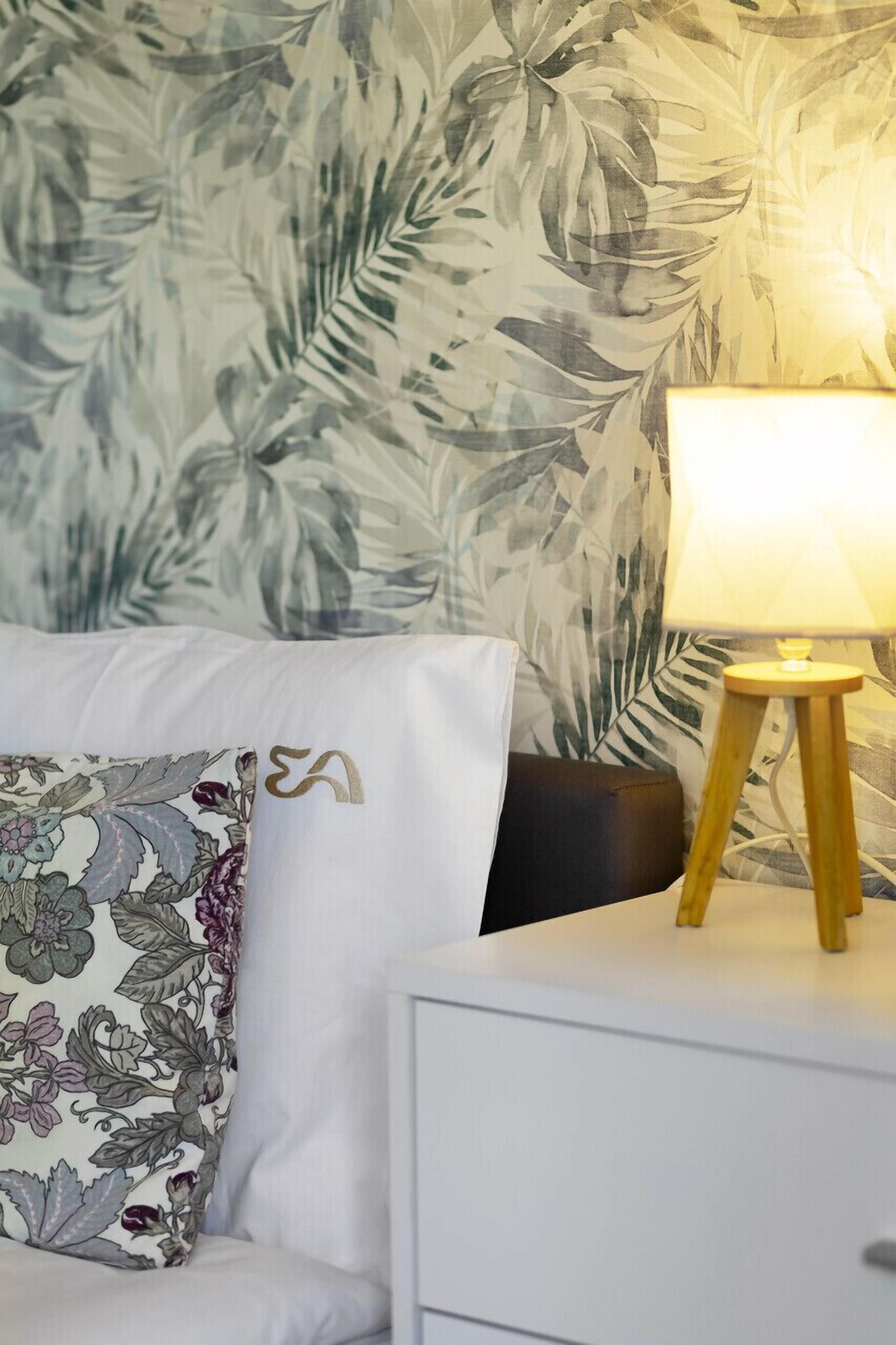 Uma cama com travesseiro estampado e mesa de cabeceira com abajur.