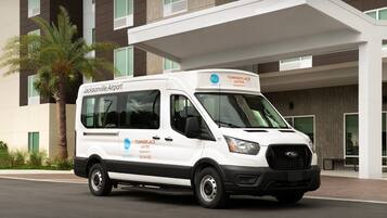 Uma van branca com a inscrição "TOWNEPLACE SUITES MARRIOTT" e "Jacksonville Airport", estacionada em frente a um moderno edifício de hotel.