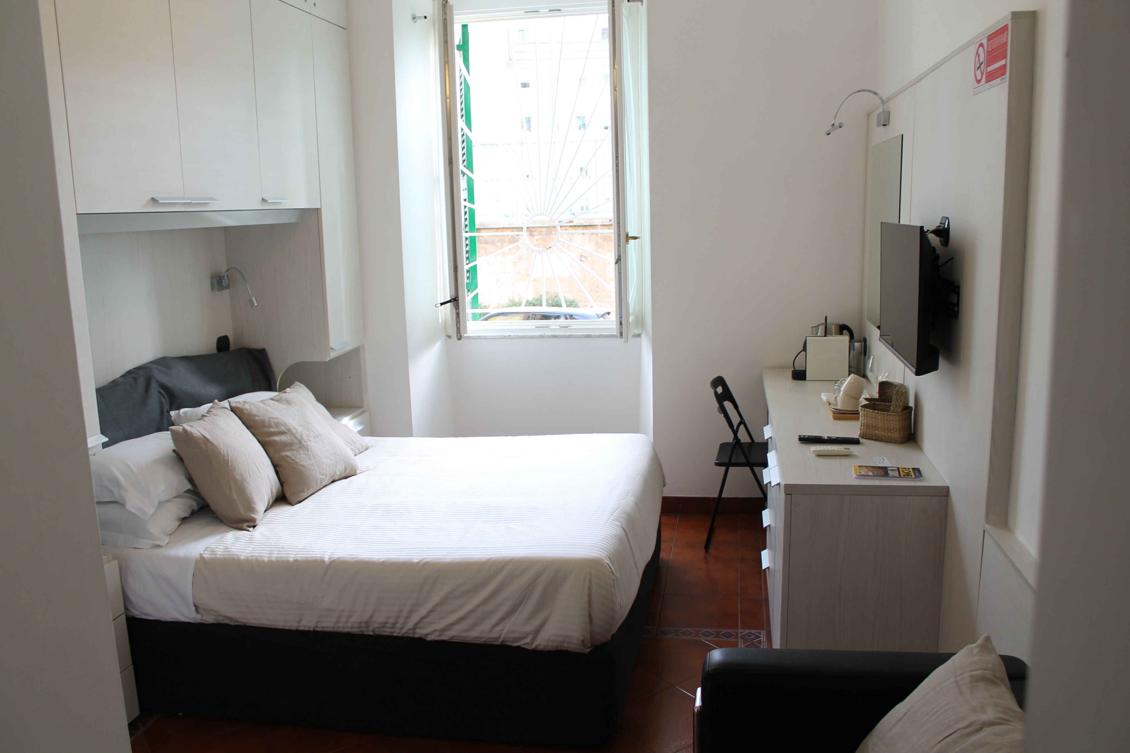 Quarto com cama, escrivaninha, cadeira, televisão e janela.