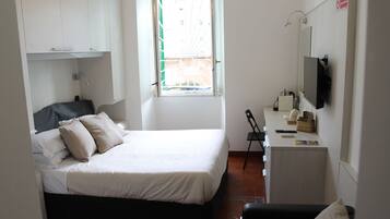 Quarto com cama, escrivaninha, cadeira, televisão e janela.