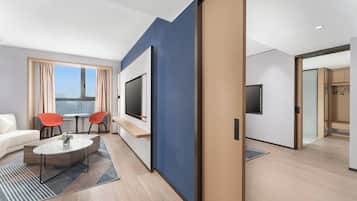 Quarto de hotel moderno com sofá, duas cadeiras, mesa de centro, televisão e porta deslizante para um armário.