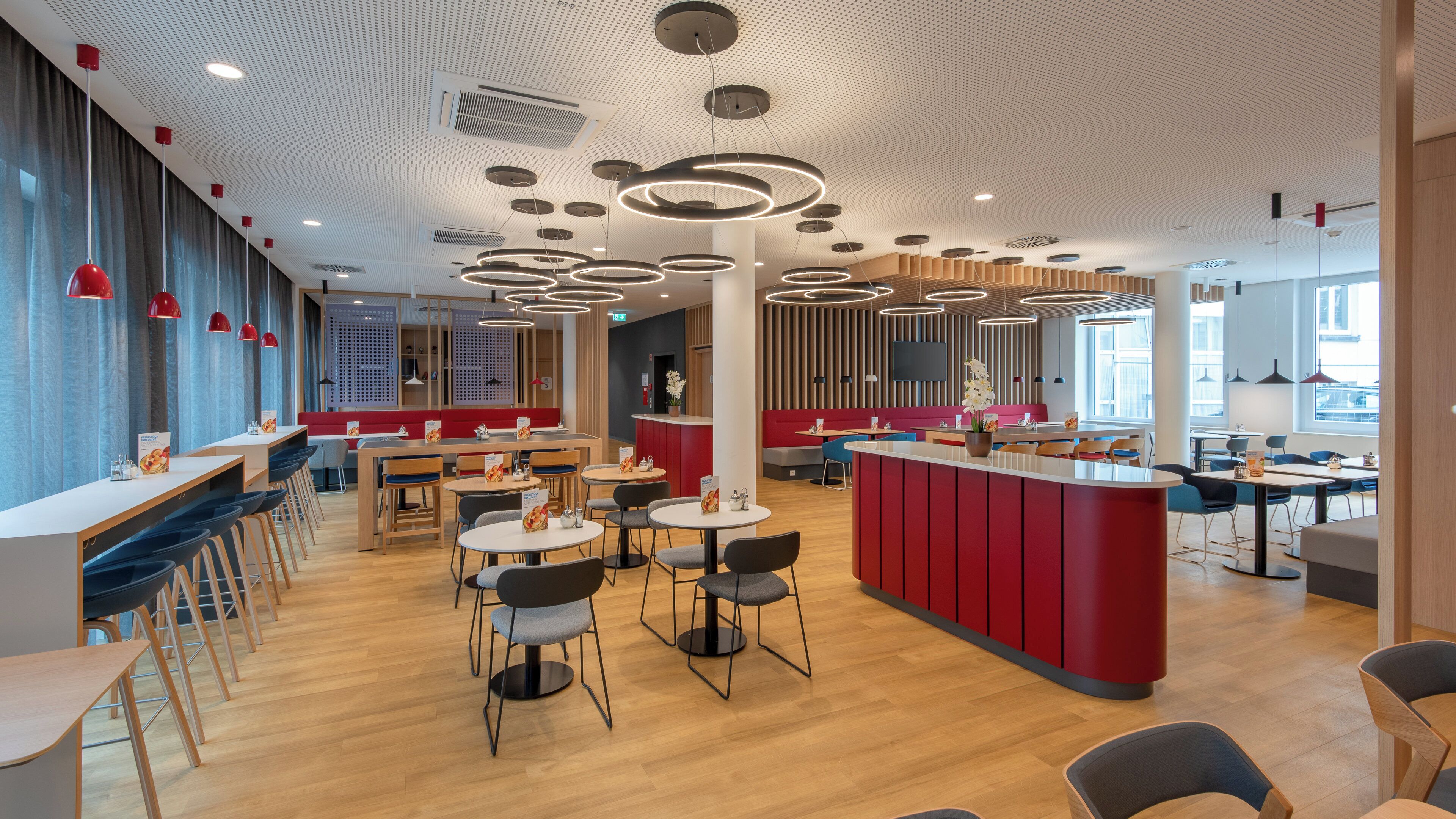 Um restaurante moderno com mesas redondas, detalhes em vermelho e piso de madeira.