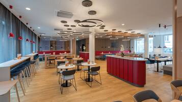 Um restaurante moderno com mesas redondas, detalhes em vermelho e piso de madeira.