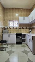Uma cozinha compacta com papel de parede estampado, fogão a gás, armários brancos e uma pequena janela.