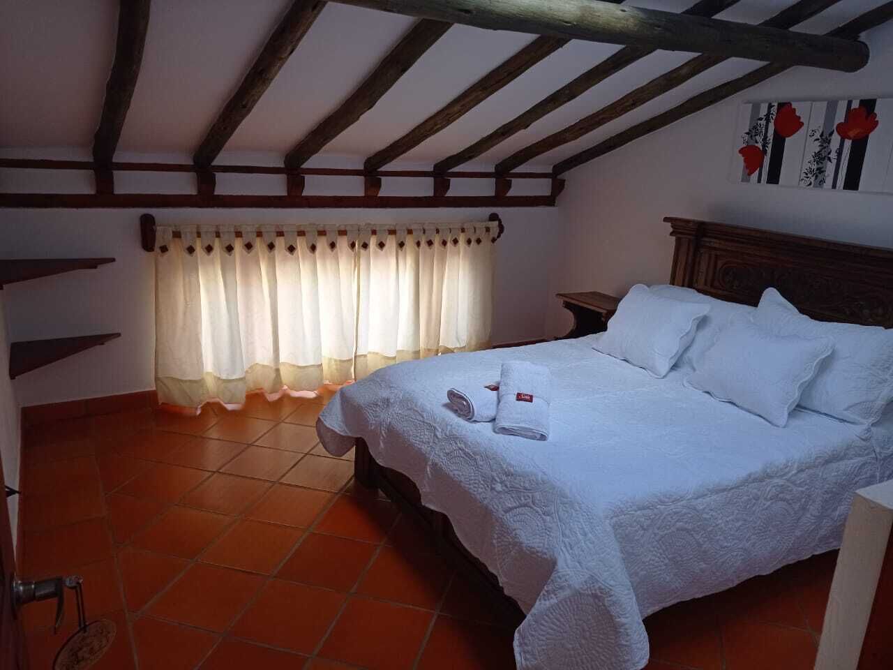 Quarto com cama, mesa de cabeceira, janela com cortinas e chão de azulejos.