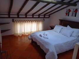 Quarto com cama, mesa de cabeceira, janela com cortinas e chão de azulejos.